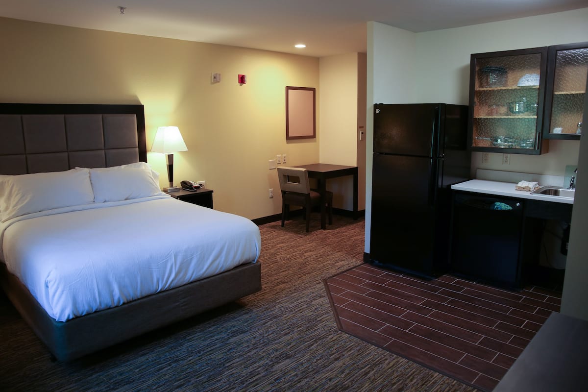 Quarto de hotel com cama, escrivaninha, refrigerador e pia.
