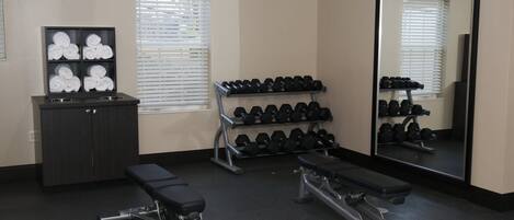 Uma academia com equipamentos de ginástica, um banco e um espelho.