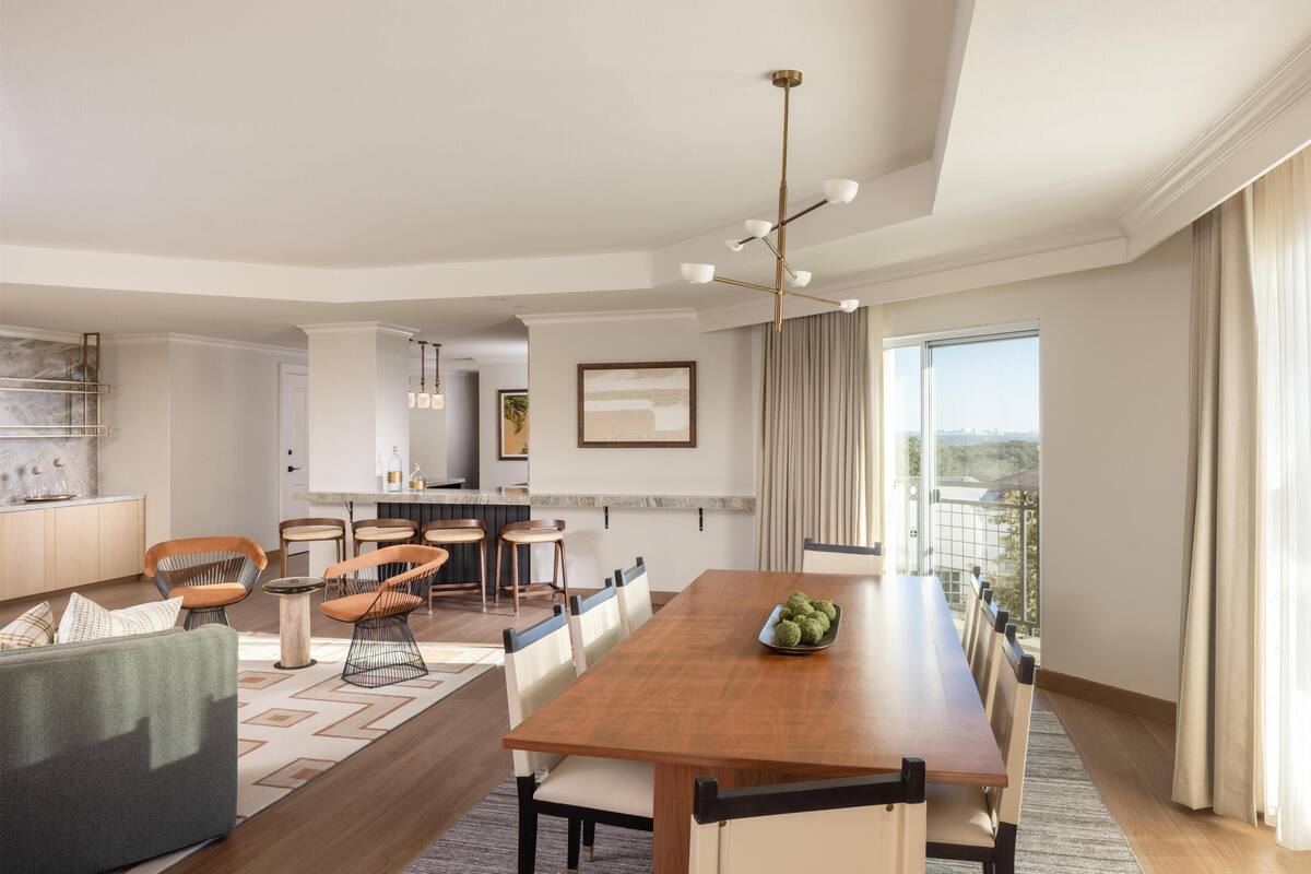 Quarto de hotel moderno com área de refeições, cozinha e varanda com vista para a cidade.