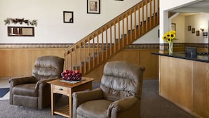 Um hall com duas poltronas de couro, uma mesa de madeira com um vaso de girassóis e uma escada com corrimãos de madeira.