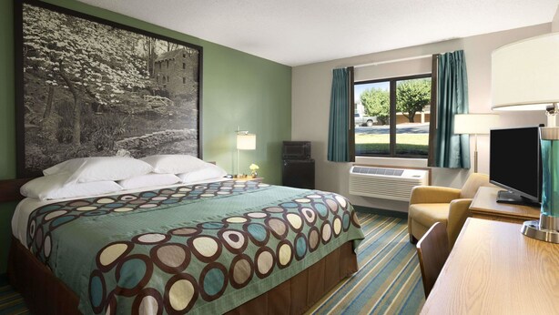 Quarto de hotel com cama, escrivaninha, cadeira, televisão e janela com cortinas.