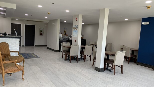 Uma ampla área de refeições com várias mesas e cadeiras, um balcão de recepção e uma cozinha ao fundo.