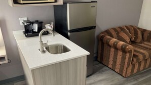 Uma cozinha compacta com pia embutida, geladeira de aço inoxidável e sofá listrado.