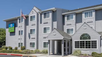 Um hotel de vários andares com design moderno, exibindo o logotipo SureStay em destaque e uma bandeira americana.