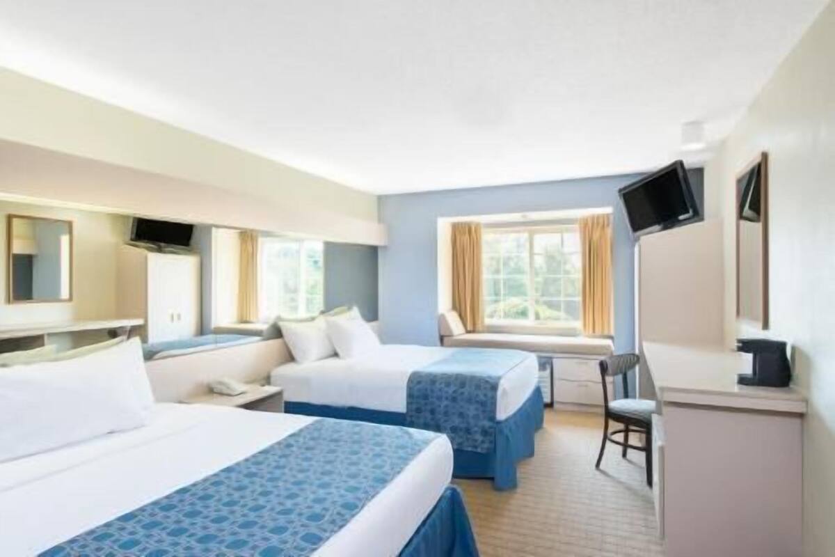 Quarto de hotel com duas camas, uma escrivaninha, uma cadeira, uma televisão e uma janela.