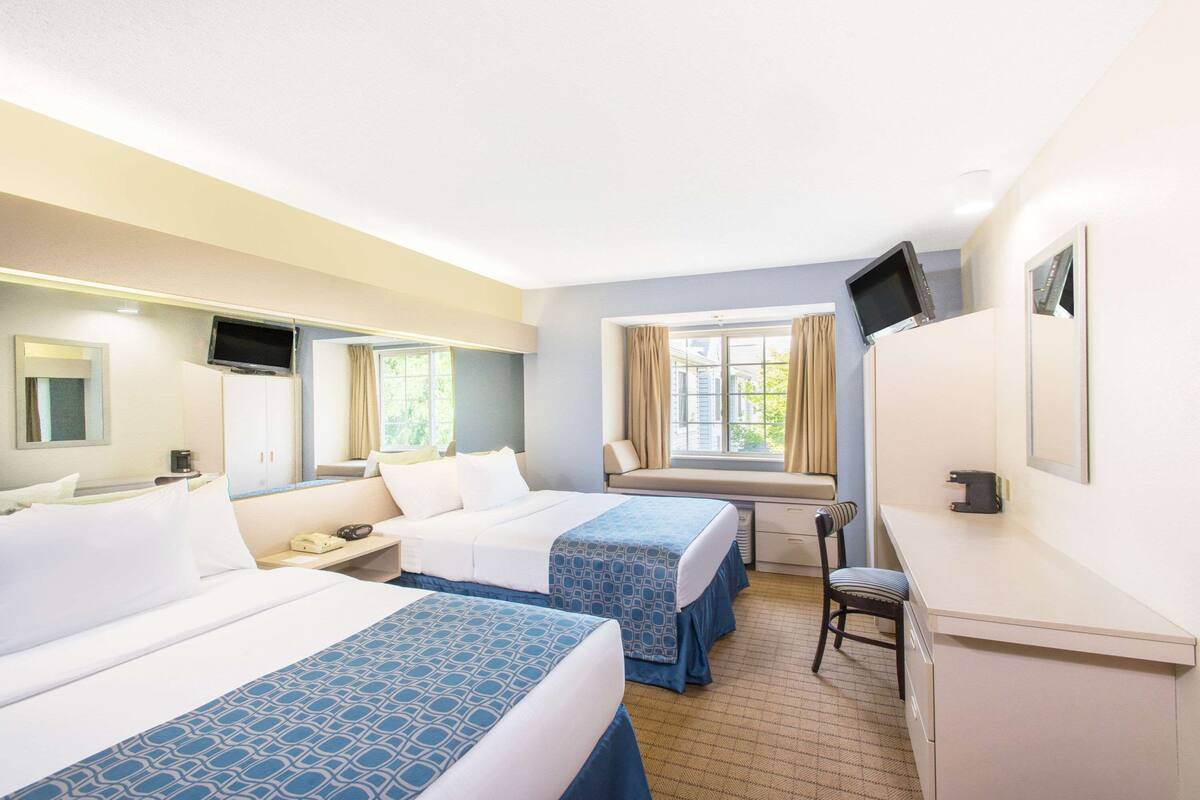 Quarto de hotel com duas camas, uma mesa, uma cadeira, uma televisão e uma janela com cortinas.