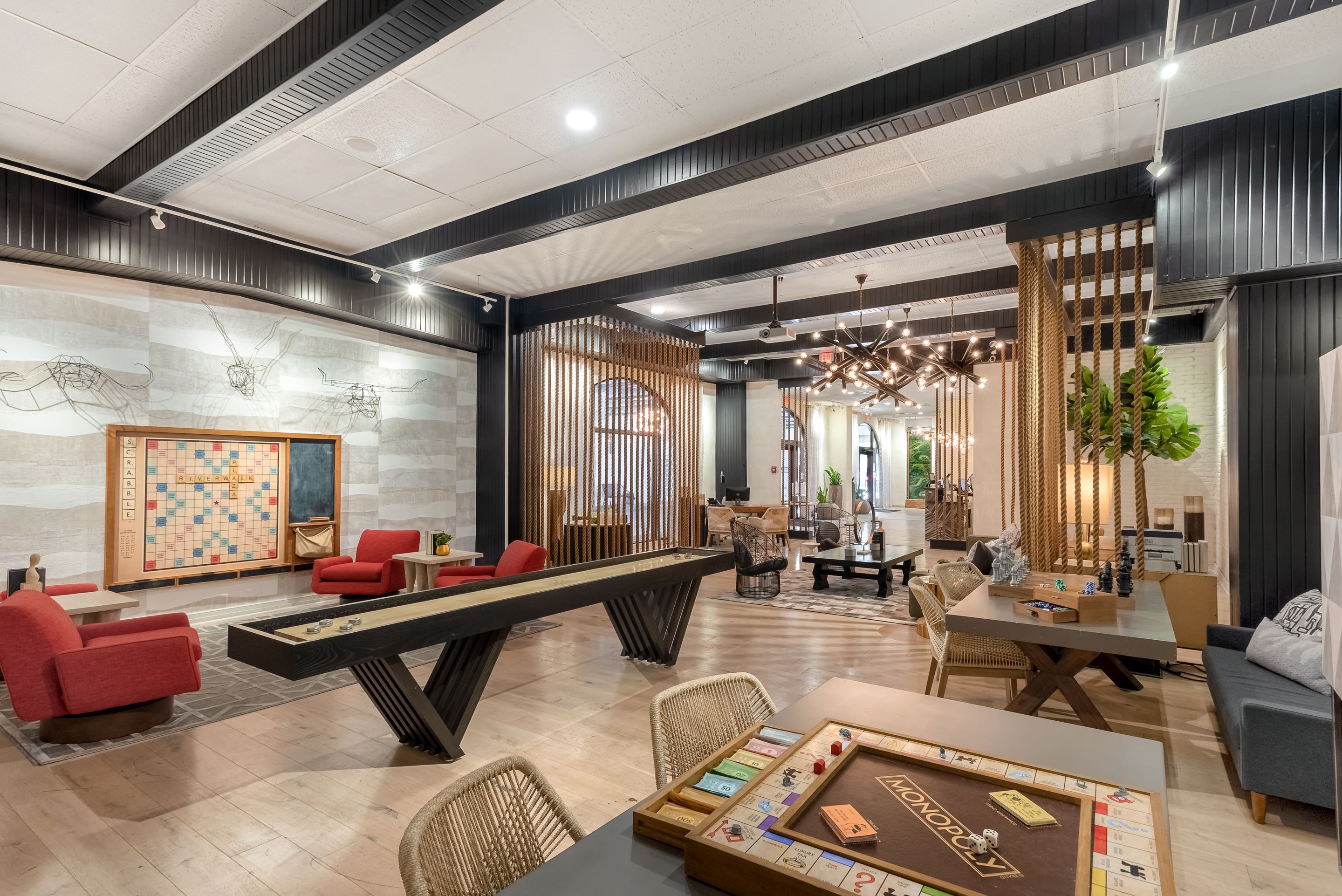 Uma área de estar moderna com uma mesa de shuffleboard grande, assentos vermelhos e diversos jogos de tabuleiro.