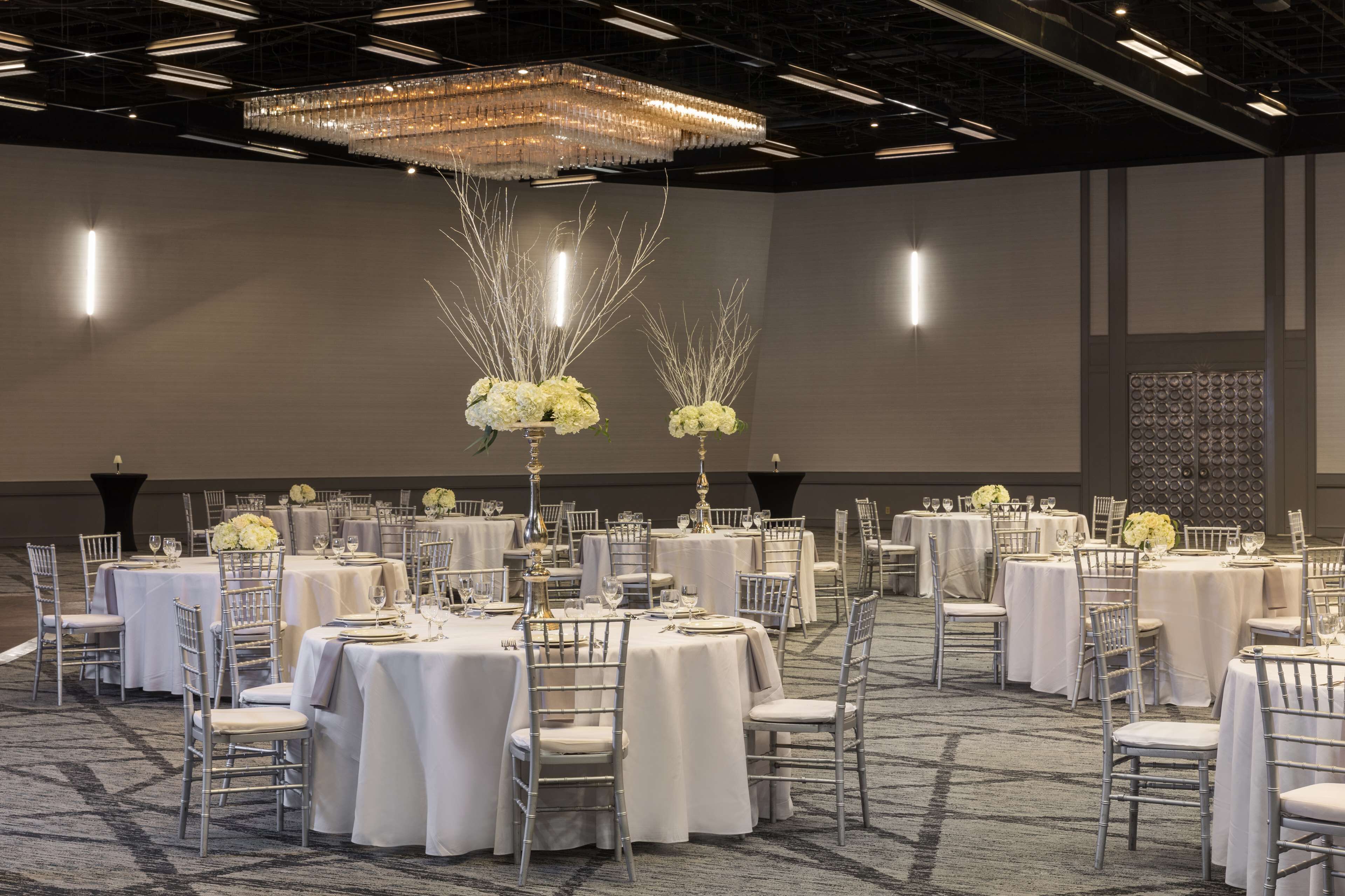 Uma sala de banquetes com mesas redondas, toalhas brancas e cadeiras de prata.