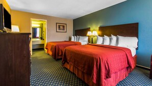 Quarto de hotel com duas camas, uma escrivaninha, televisão e banheiro visível por uma porta aberta.