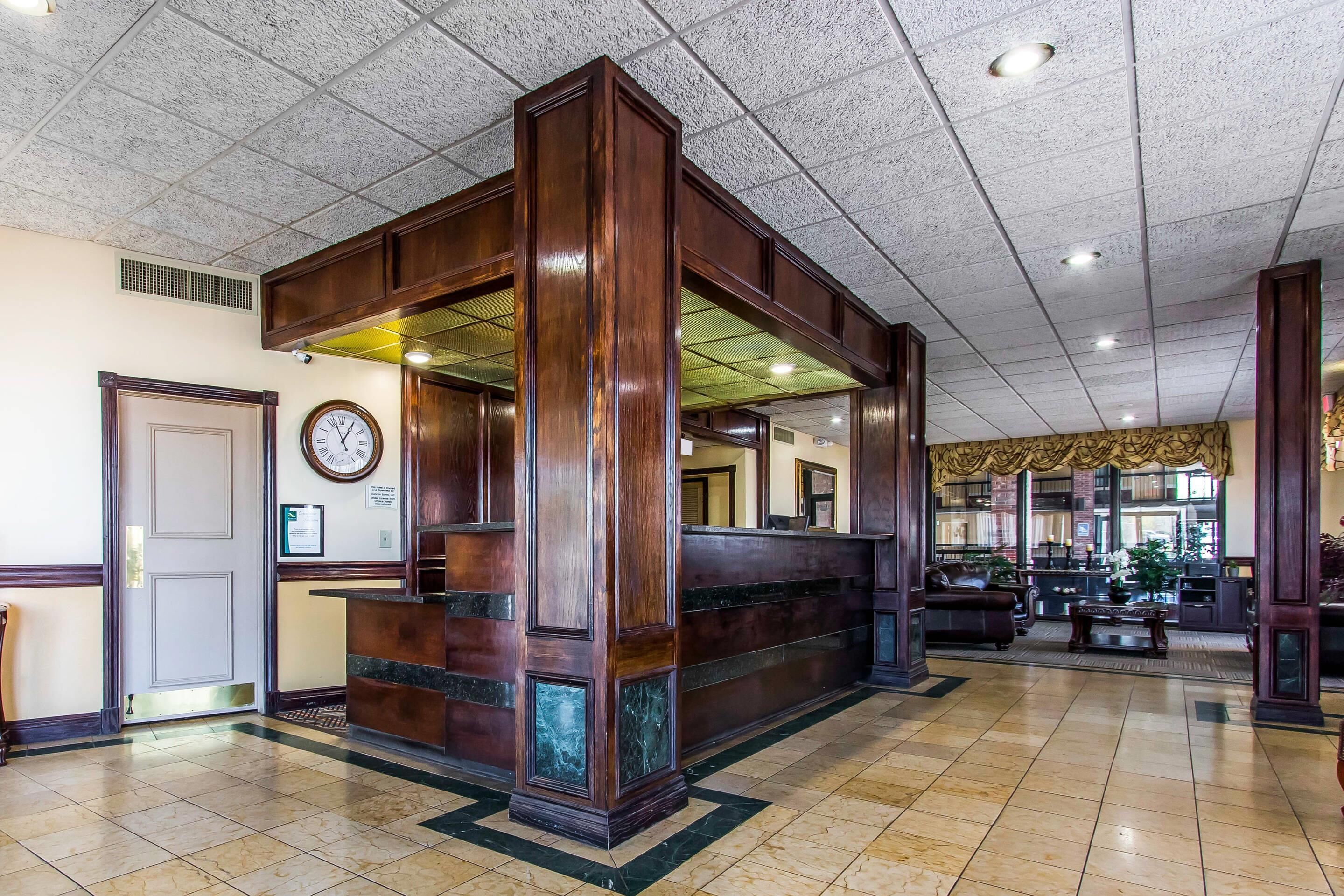Uma área de recepção com um balcão de madeira, um relógio e vista para uma sala de estar com lareira.
