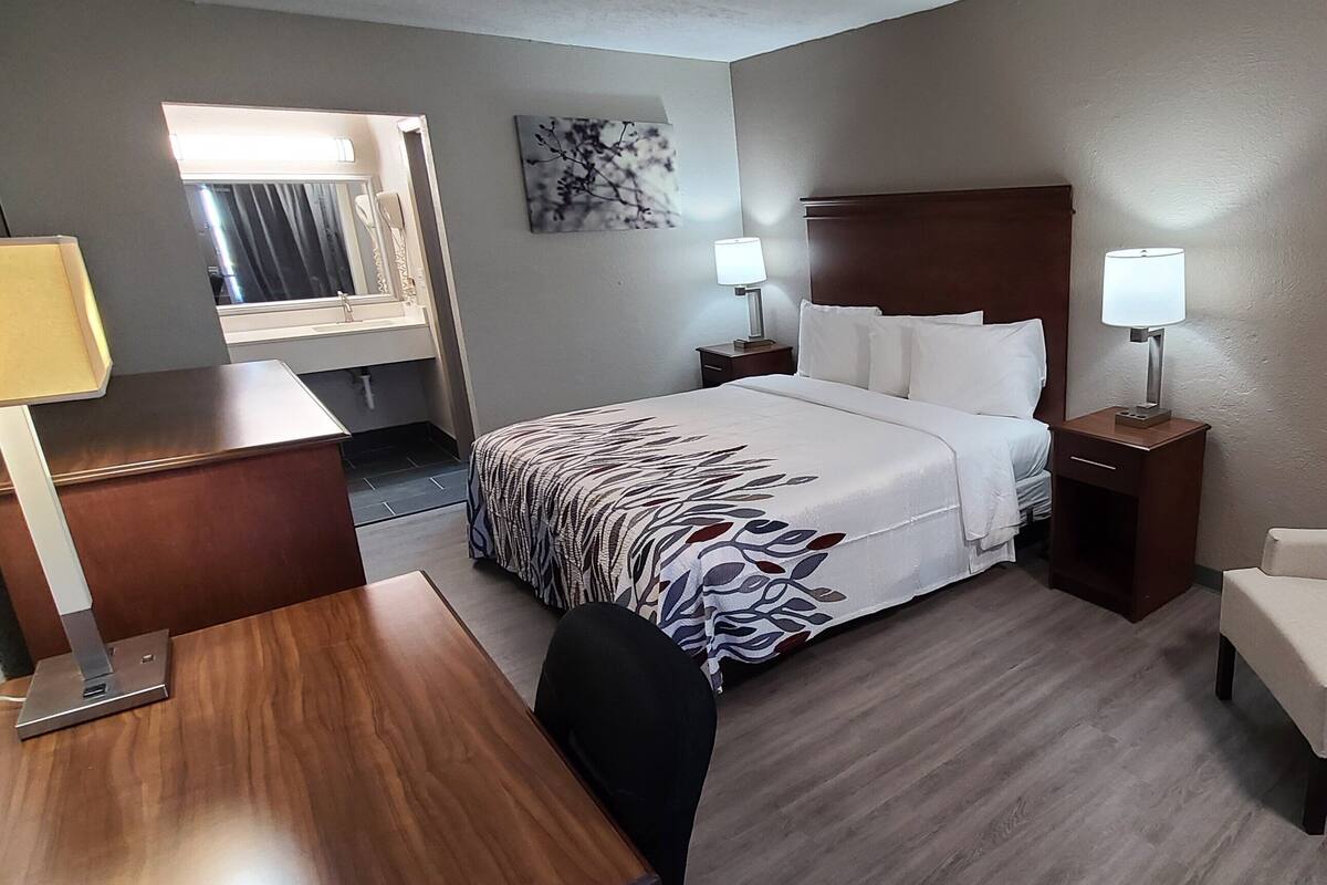Quarto de hotel com uma cama, mesas de cabeceira com luminárias, uma escrivaninha, uma cadeira e um sofá.