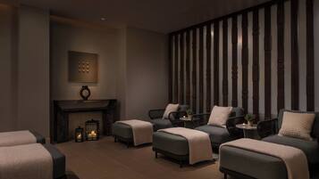 Uma sala de spa moderna com lareira, dois sofás e uma parede com ripas de madeira verticais.