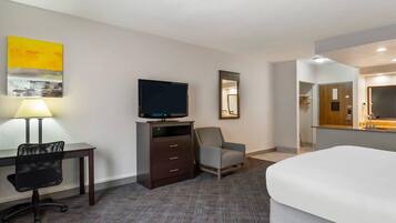Quarto de hotel com cama, escrivaninha, cadeira, televisão, cômoda e espelho.