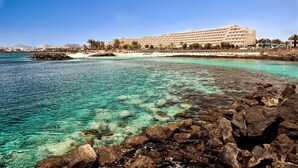 Um hotel à beira-mar com um edifício grande, águas turquesa cristalinas e costa rochosa.