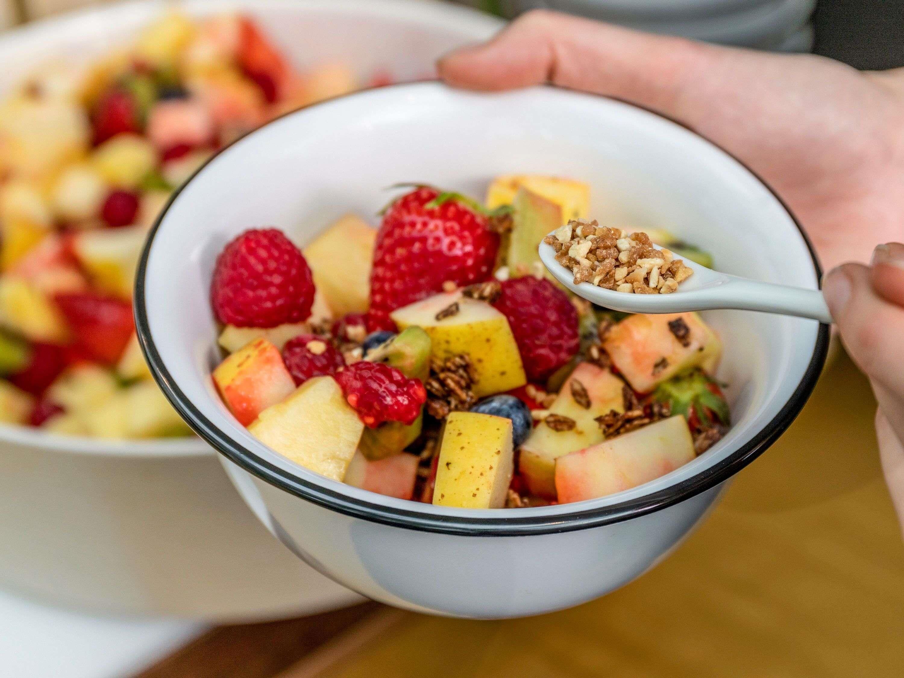 Uma tigela de salada de frutas com uma colherada de granola.