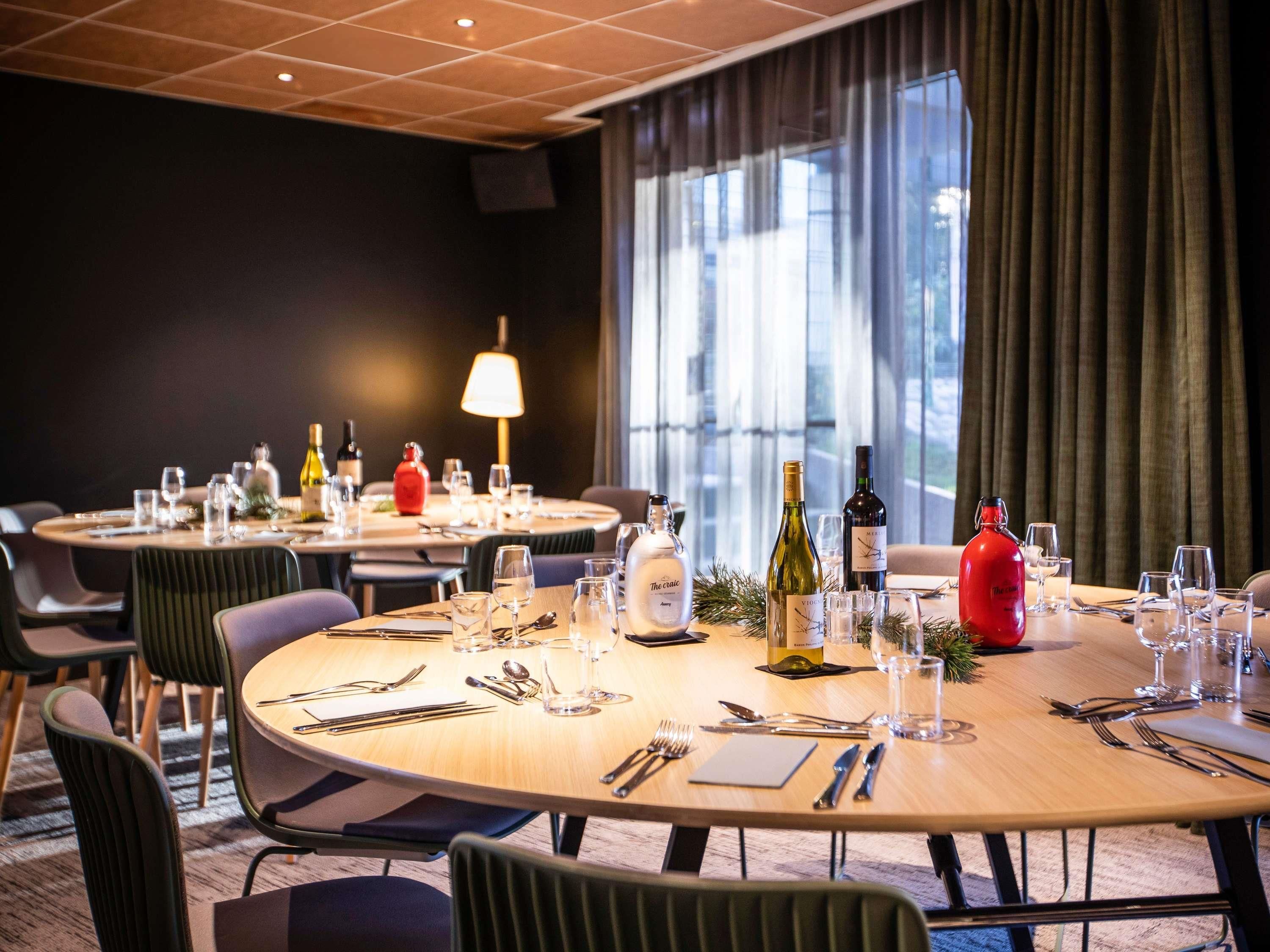 Uma área de refeições de hotel com mesas redondas preparadas para servir, equipada com copos de vinho, garrafas e talheres.