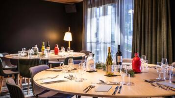 Uma área de refeições de hotel com mesas redondas preparadas para servir, equipada com copos de vinho, garrafas e talheres.