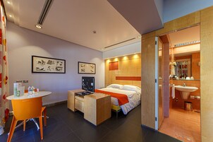 Quarto de hotel moderno com cama, escrivaninha e banheiro.