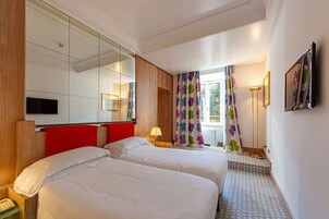 Quarto de hotel com duas camas, um espelho grande, televisão e janela com cortinas.