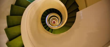 Escadaria em espiral com degraus verdes e um corrimão central.