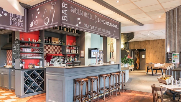 Uma área de bar com balcão, banquetas e prateleiras cheias de garrafas e copos.