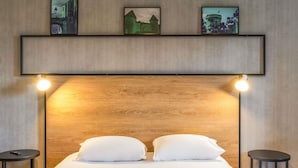 Quarto de hotel com cabeceira de madeira, duas mesas de cabeceira, cama com roupa de cama branca e três quadros na parede.