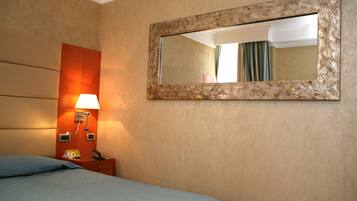 Quarto de hotel com cama, mesa de cabeceira com abajur, telefone e espelho na parede.