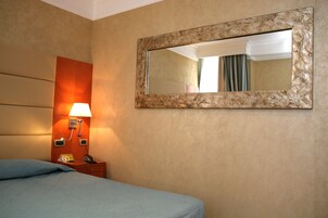 Quarto de hotel com cama, mesa de cabeceira com abajur, telefone e espelho na parede.