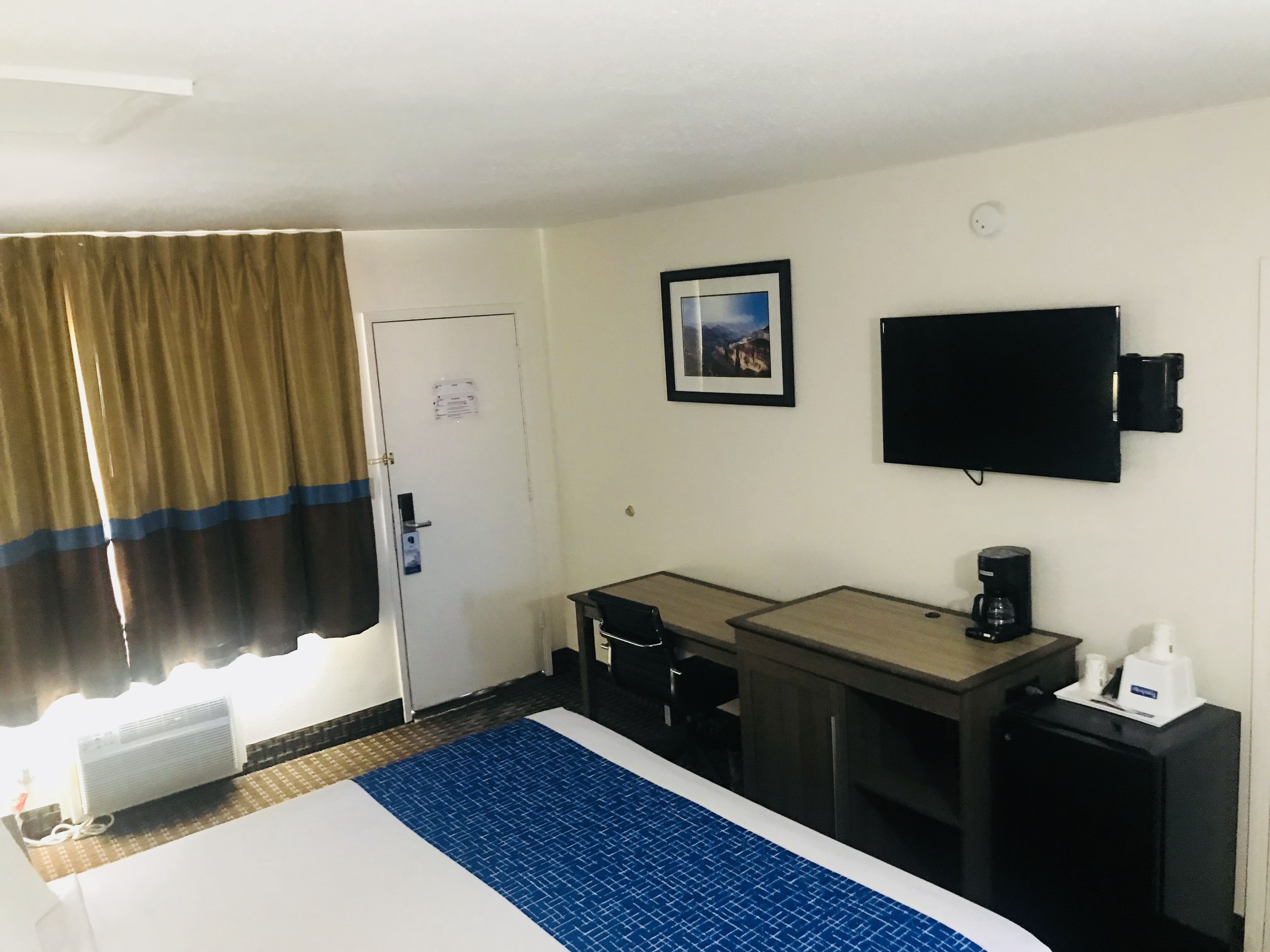 Quarto de hotel com cama, escrivaninha, cadeira, televisão e máquina de café.