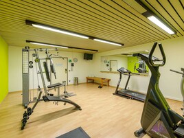 Uma academia com equipamentos de exercício, um espelho, um banco e um relógio na parede.