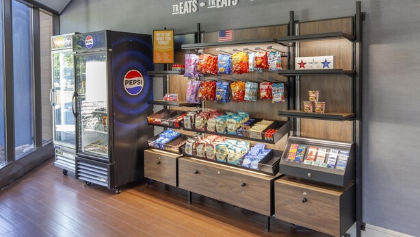 Exposição de petiscos com diferentes tipos de batatas fritas e lanches, um refrigerador de Pepsi e uma placa indicando guloseimas.