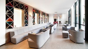 Uma área de lounge moderna com um sofá comprido, assentos acolchoados e um painel de parede com padrão geométrico.