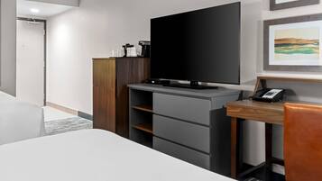Quarto de hotel moderno com televisão de tela plana presa a uma escrivaninha de madeira, uma cama, um guarda-roupa e um pequeno espaço de estar.