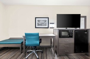 Quarto de hotel compacto com uma cama de solteiro, escrivaninha com cadeira, televisão, micro-ondas e frigorífico.