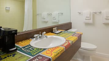 Um banheiro com pia, vaso sanitário e espelho. A pia está sobre uma bancada com diversos anúncios.