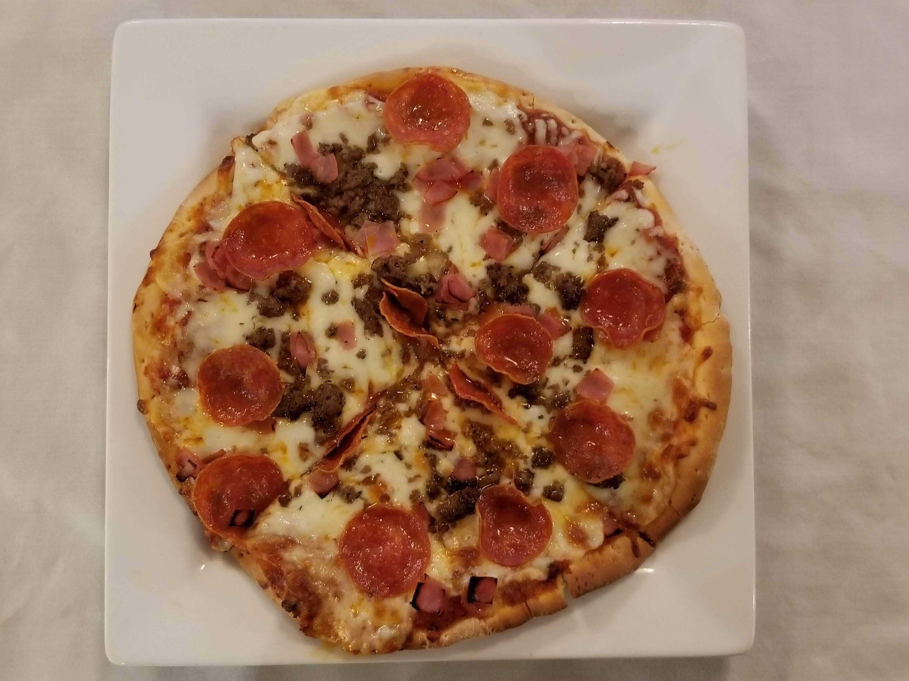 Pizza com cobertura de pepperoni e fiambre, sobre um prato branco.