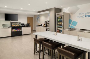 Um café moderno com um balcão comprido, banquetas, uma máquina de café e um refrigerador cheio de bebidas.