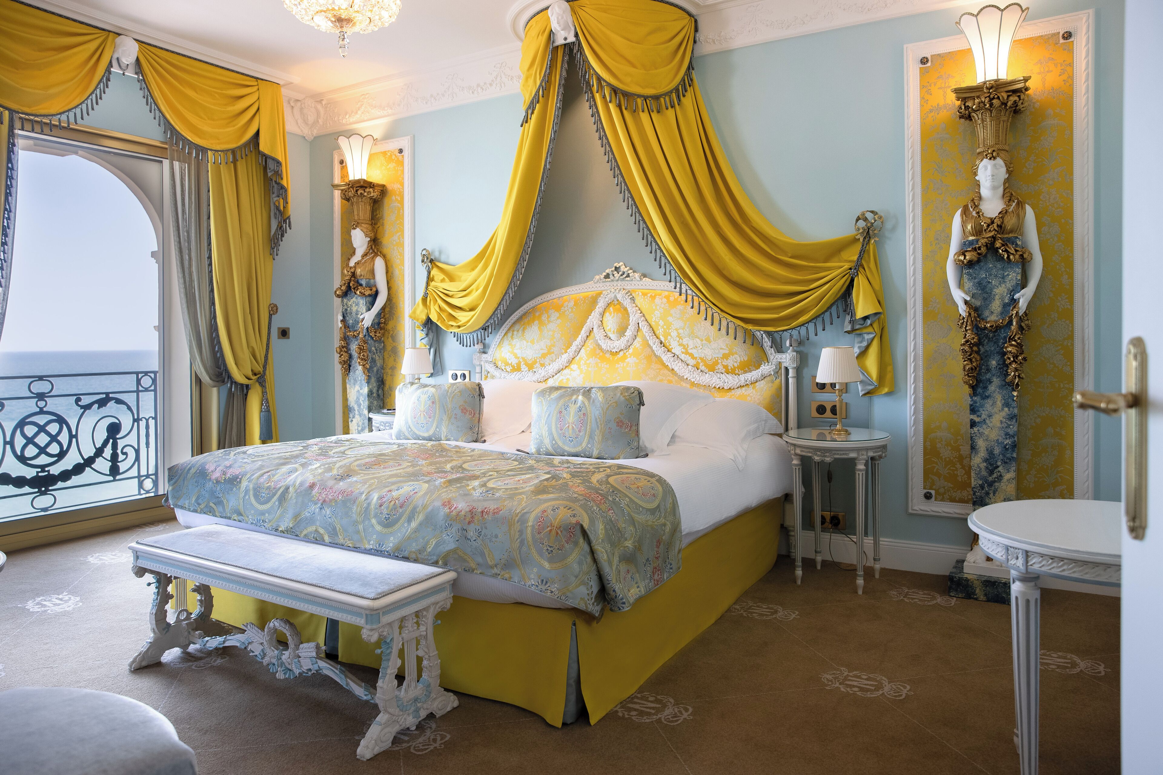 Quarto com cama grande, um banco, mesa de cabeceira, luminária e um ornamento na parede.