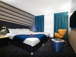 Quarto de hotel moderno com uma cama grande, uma escrivaninha, uma cadeira e uma televisão.