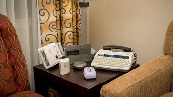 Quarto de hotel com uma escrivaninha que apresenta uma máquina de escrever antiga, um projetor moderno e um pequeno alto-falante.