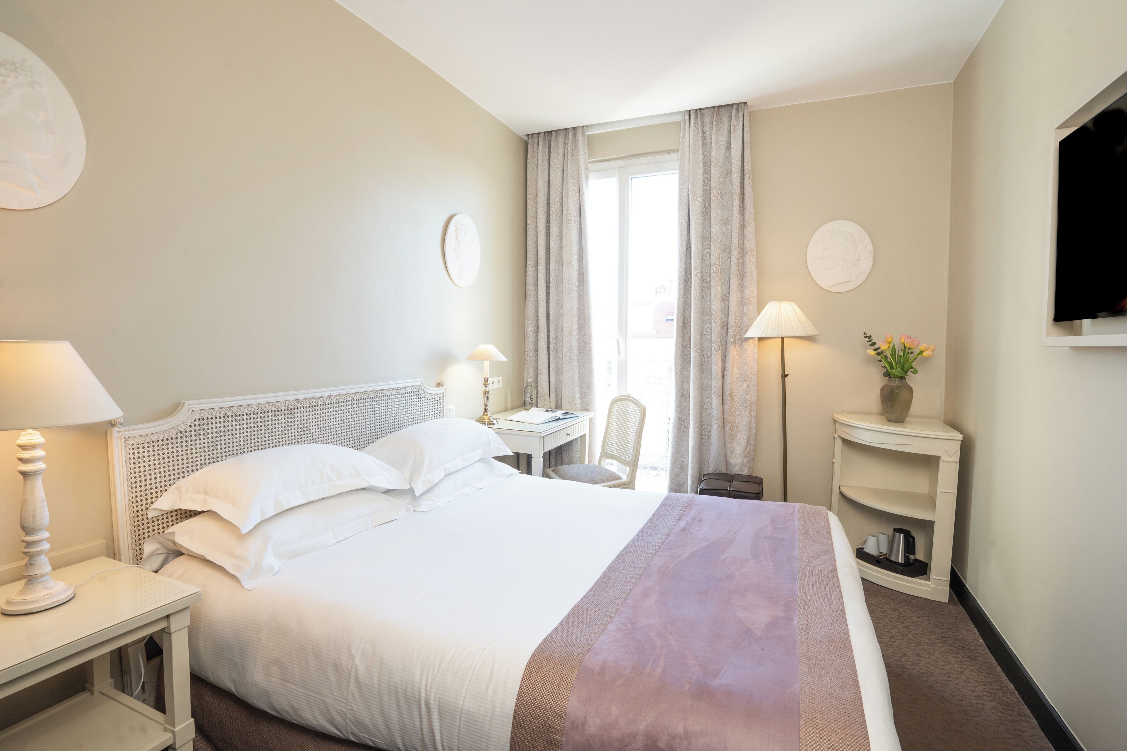 Quarto de hotel com cama, mesas de cabeceira, escrivaninha, cadeira, televisão e janela com cortinas.