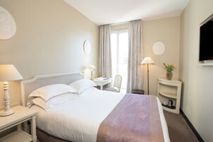 Quarto de hotel com cama, mesas de cabeceira, escrivaninha, cadeira, televisão e janela com cortinas.