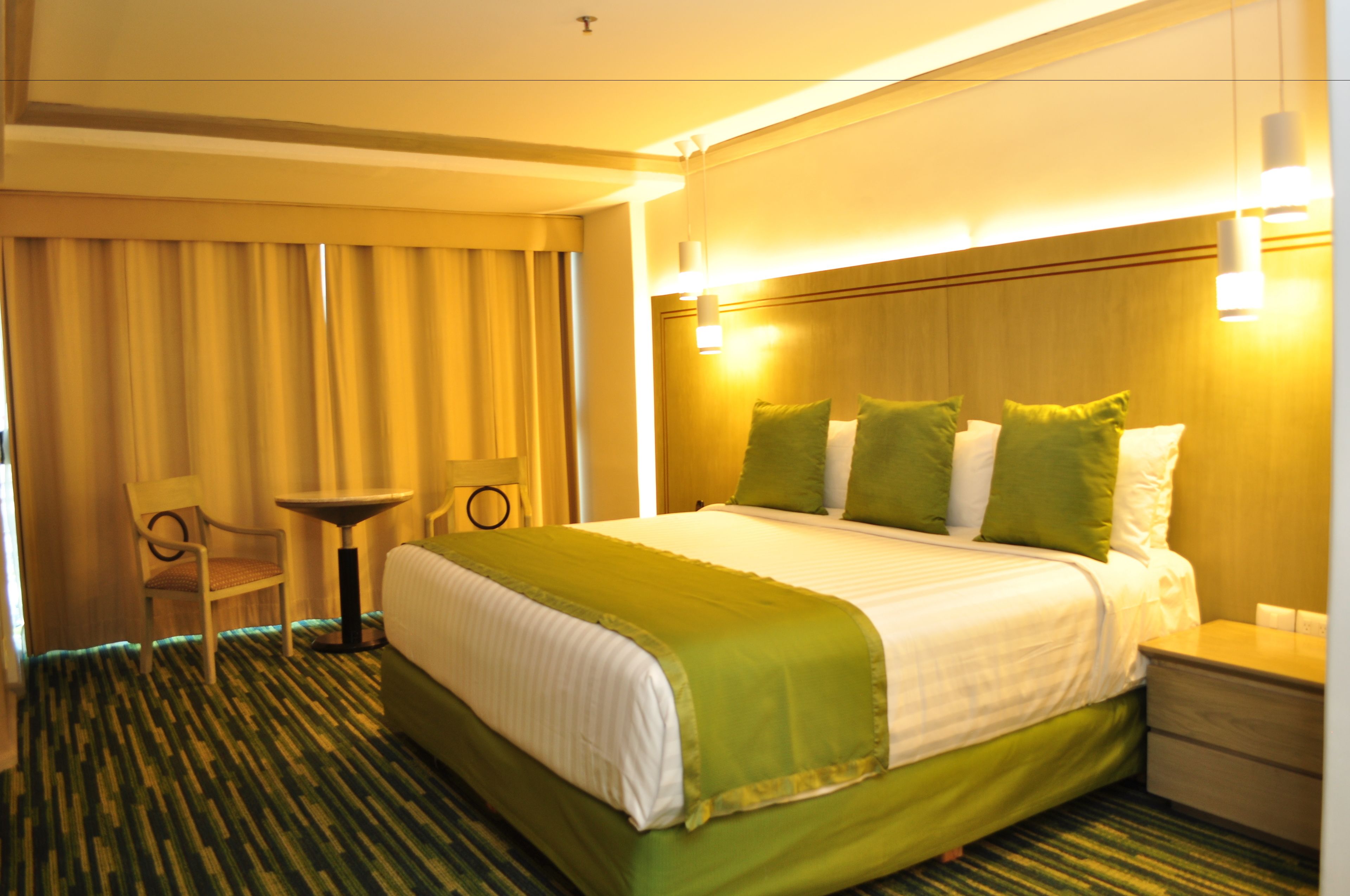 Quarto de hotel com uma cama grande, mesa de cabeceira, cadeira e pequena mesa.
