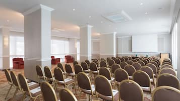 Uma sala de conferências com fileiras de cadeiras, uma tela de projetor e um espaço para apresentações.