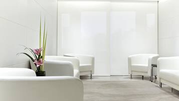 Um hall de hotel moderno e minimalista, com uma grande luminária circular no teto, um balcão de recepção e duas áreas de estar com sofás brancos.