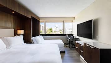 Quarto de hotel com duas camas, uma escrivaninha, televisão e vista para a cidade.