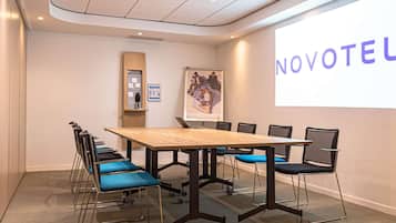 Uma sala de conferência com uma mesa comprida, cadeiras, um projetor e uma tela exibindo 'NOVOTEL'.