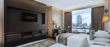 Quarto de hotel com duas camas, televisão presa na parede, mesa de trabalho com abajur e vista para o horizonte da cidade.