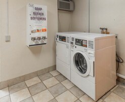 Uma lavanderia com máquina de lavar de carregamento frontal e painel de controle fixado na parede para sabão, alvejante e amaciante.