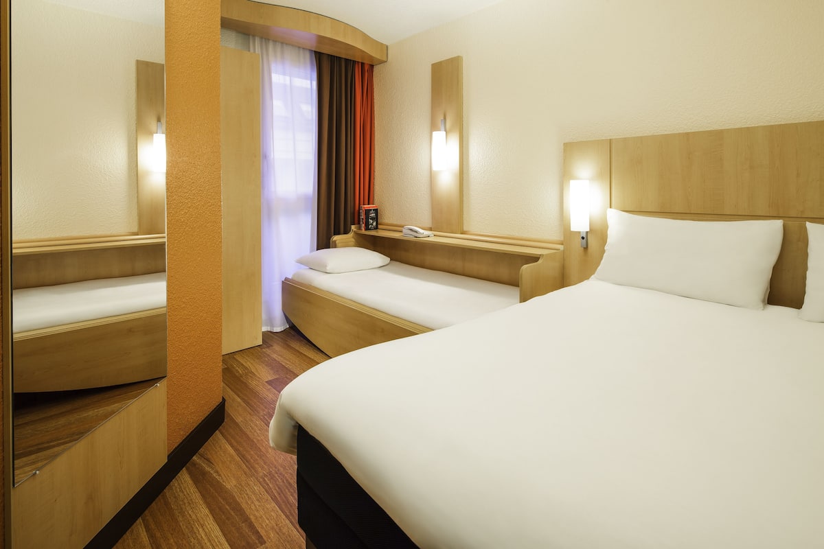 Quarto de hotel com duas camas de solteiro, cabeceira de madeira, mesa de cabeceira com luminária e um espelho.
